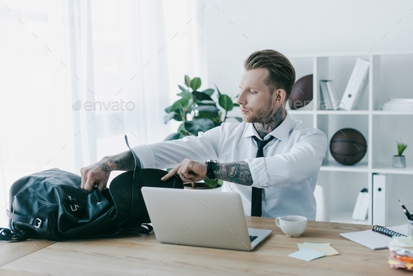young tattooed businessman opening backpack while working with laptop ...
