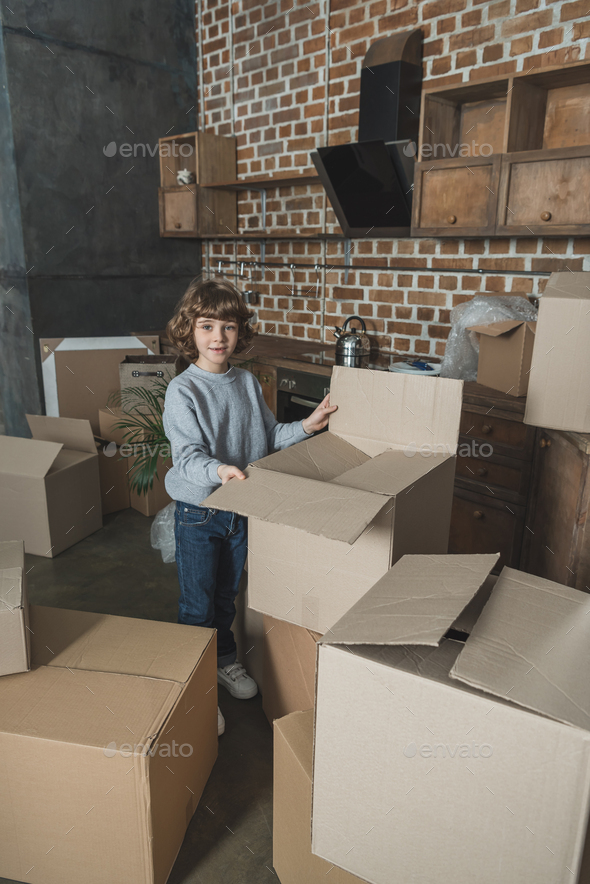 cute little boy smiling at camera while packing boxes during relocation ...