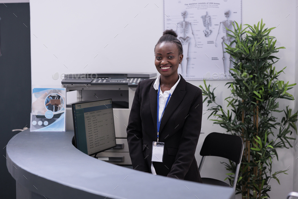 Portrait of african american receptionist standing at hospital counter ...