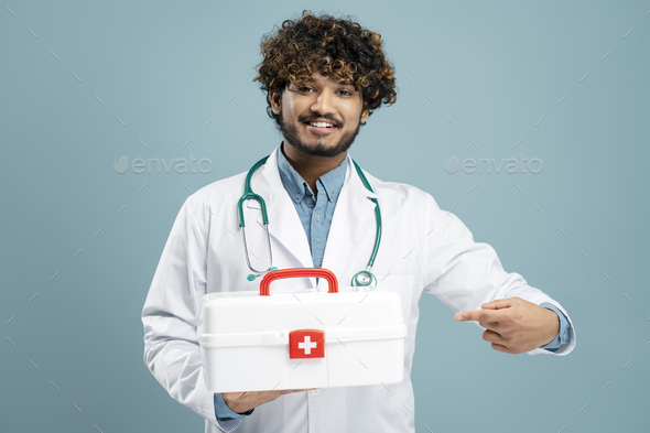 Handsome confident young Indian doctor points finger at first aid kit ...