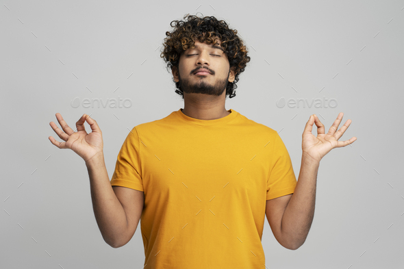 Relaxed Indian man in yellow t-shirt, meditates in zen pose with his ...