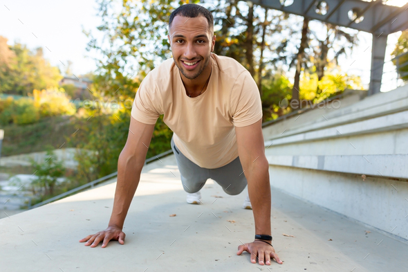 Cheerful and smiling hispanic man doing outdoor exercise in stadium ...