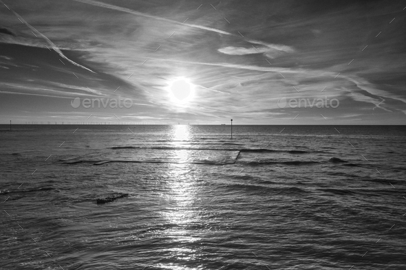 Grayscale shot of a calm sea with the bright sun reflecting on the ...