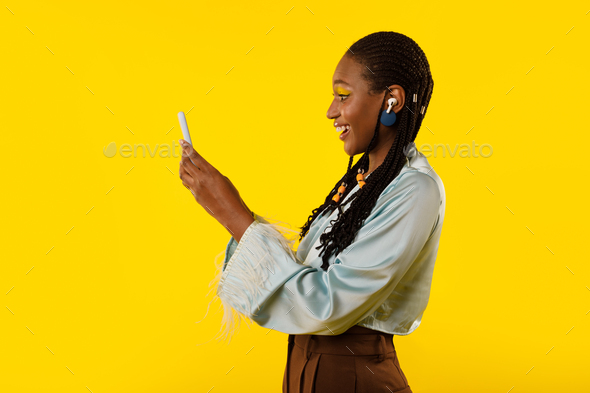 African Lady Holding Smartphone Listening Music Wearing Earbuds, Yellow Background Stock Photo ...
