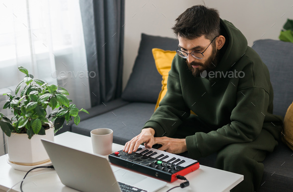 Man Recording Electronic Music Track With Portable Midi Keyboard On Laptop Computer In Home