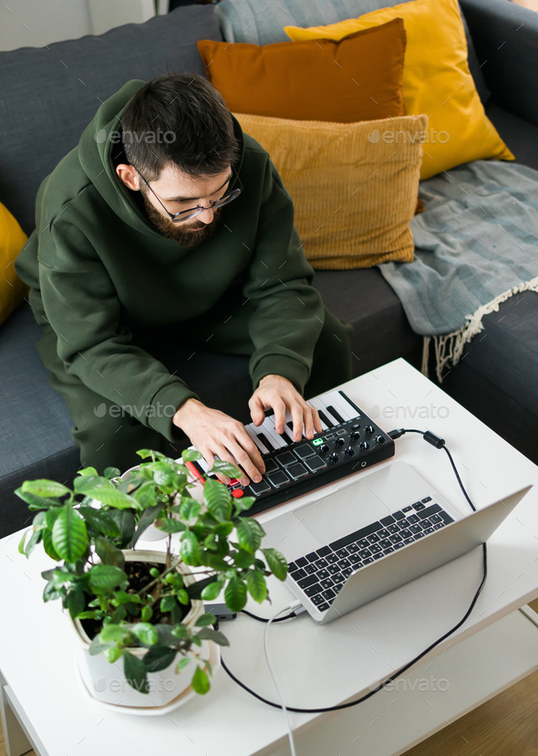 Man Recording Electronic Music Track With Portable Midi Keyboard On Laptop Computer In Home