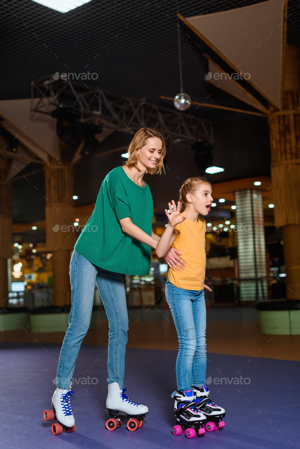 smiling mother and little daughter skating together on roller rink ...