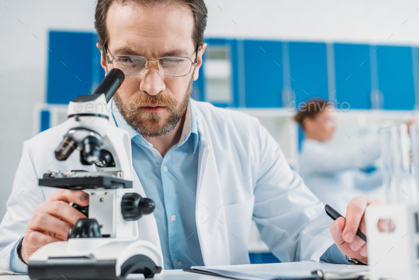 selective focus of scientist in white coat and eyeglasses looking ...