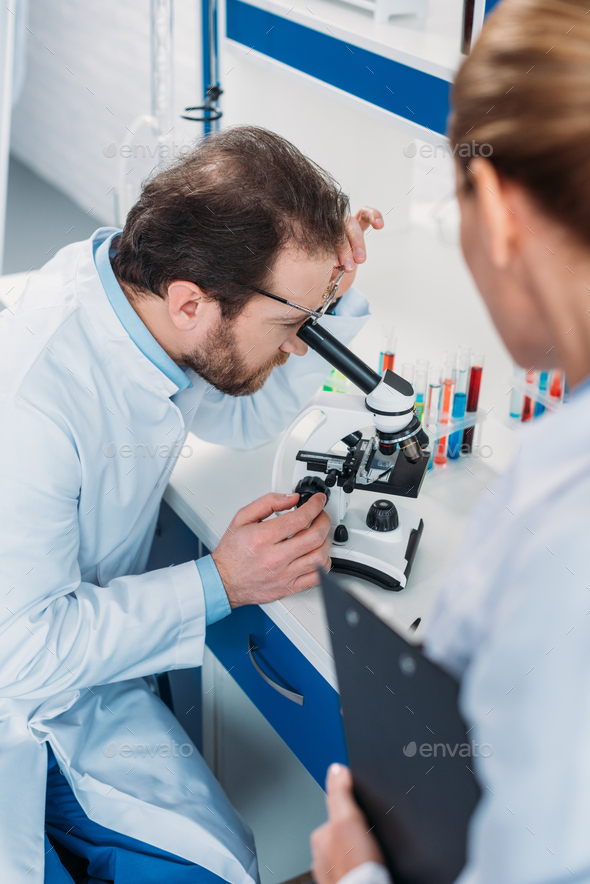 scientist in lab coat looking through microscope on reagent with ...