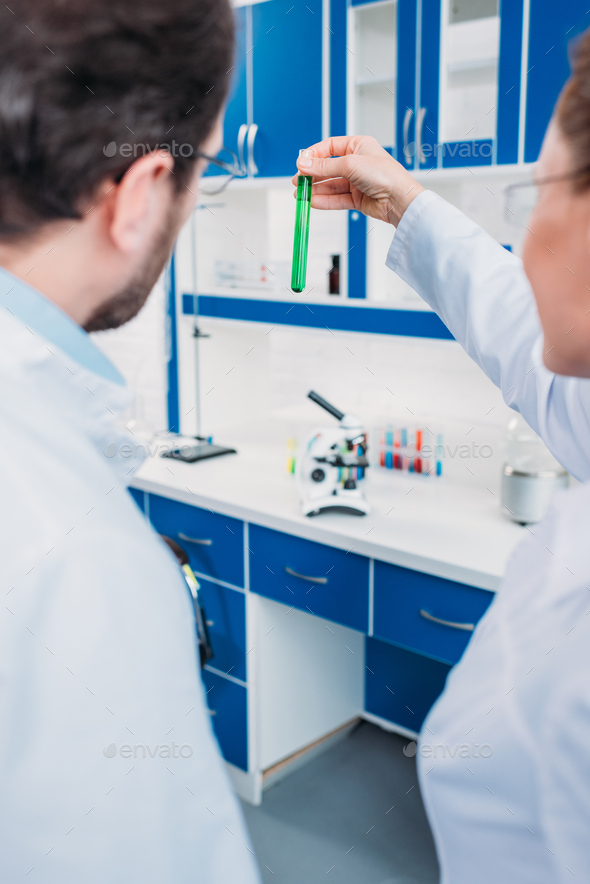 back view of scientists looking at tube with reagent in laboratory ...