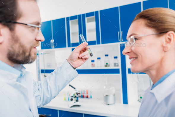 side view of scientists in eyeglasses with tube with reagent in ...