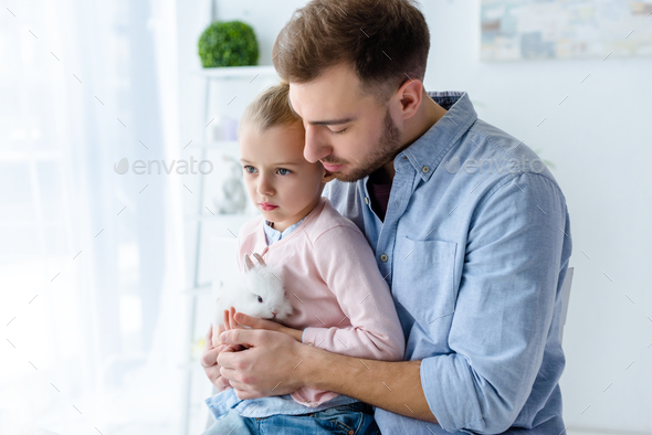Father and daughter cuddling white rabbit Stock Photo by LightFieldStudios