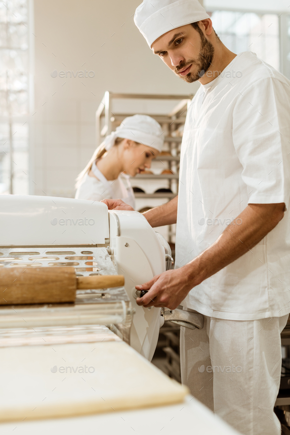 handsome baker working with industrial dough roller at baking ...