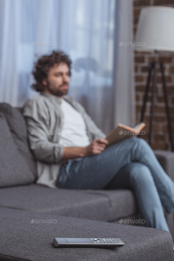 handsome man holding book with remote control on foreground Stock Photo ...