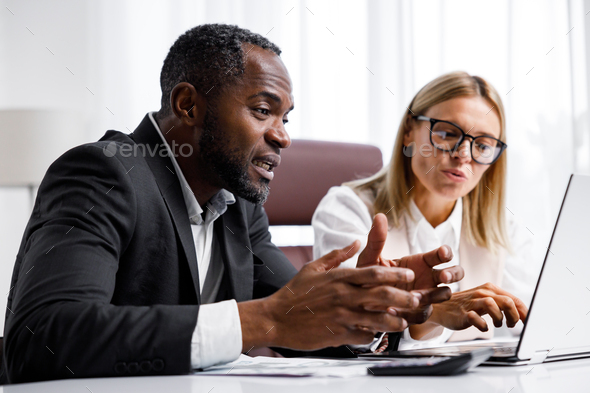 Two people analyze documents on a laptop while sitting at a table in ...