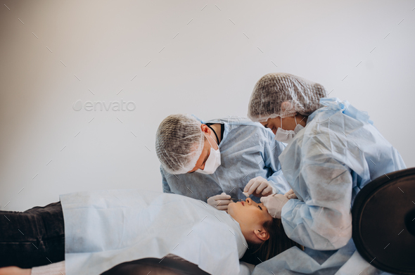 Surgeon and his assistant performing cosmetic surgery on nose in ...