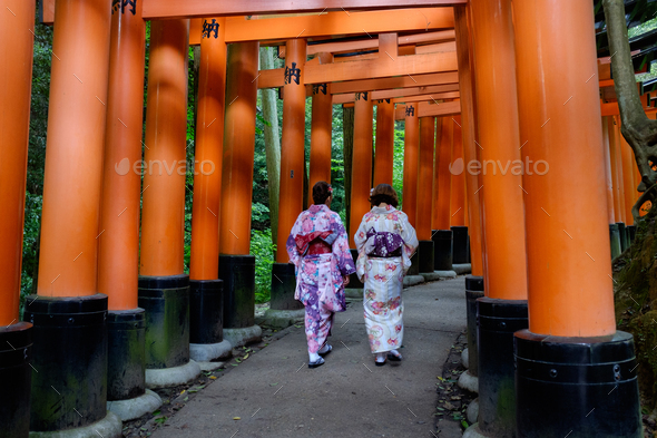 People in traditional Japanese costumes walking on the Torii path of Fushimi Inariaisha temple ...