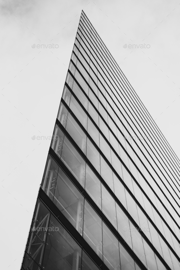 Vertical grayscale shot of a righ-rise modern glass-made office ...