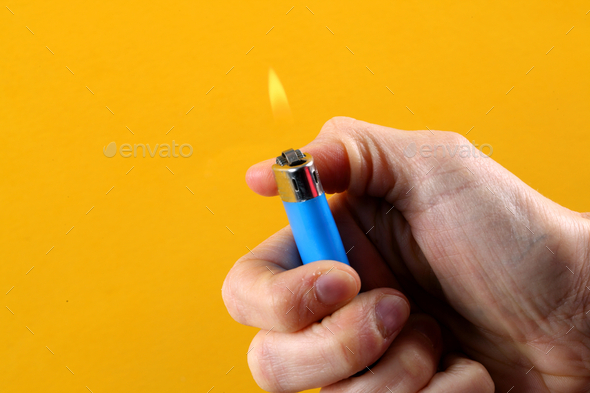 Closeup of a hand holding a burning lighter on a yellow background ...