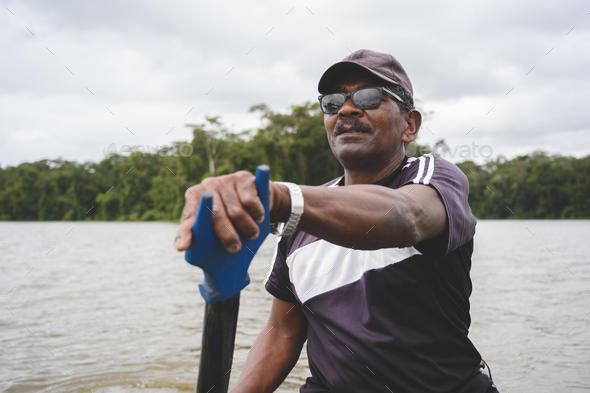 Elderly African-American male with sunglasses and cap rowing a boat on ...
