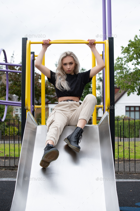 Vertical shot of a blonde Caucasian girl sitting on a slide in the ...