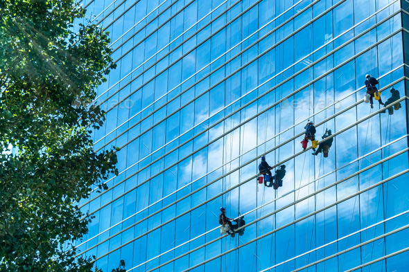 Group of cleaners in safety harness cleaning glass windows of a modern ...