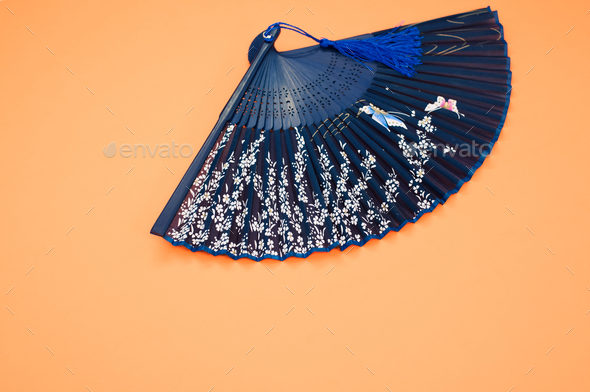 Blue hand fan with floral patterns isolated on an orange background ...
