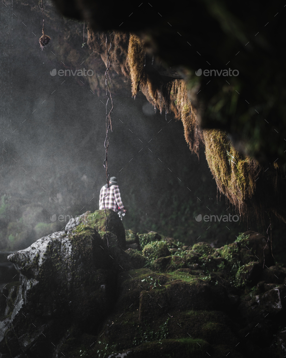 Vertical shot of a person standing near a waterfall in a forest in ...