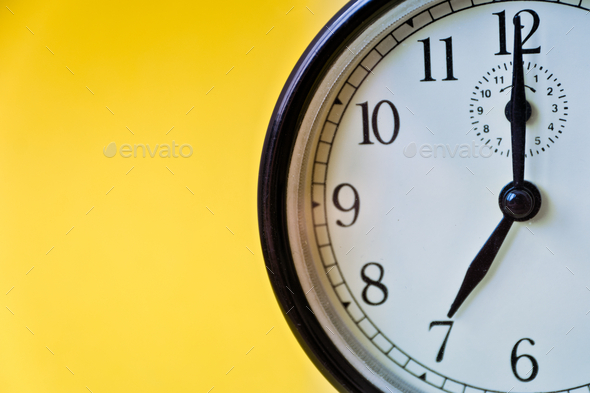 Shot of vintage retro analog clock on yellow background showing seven o ...
