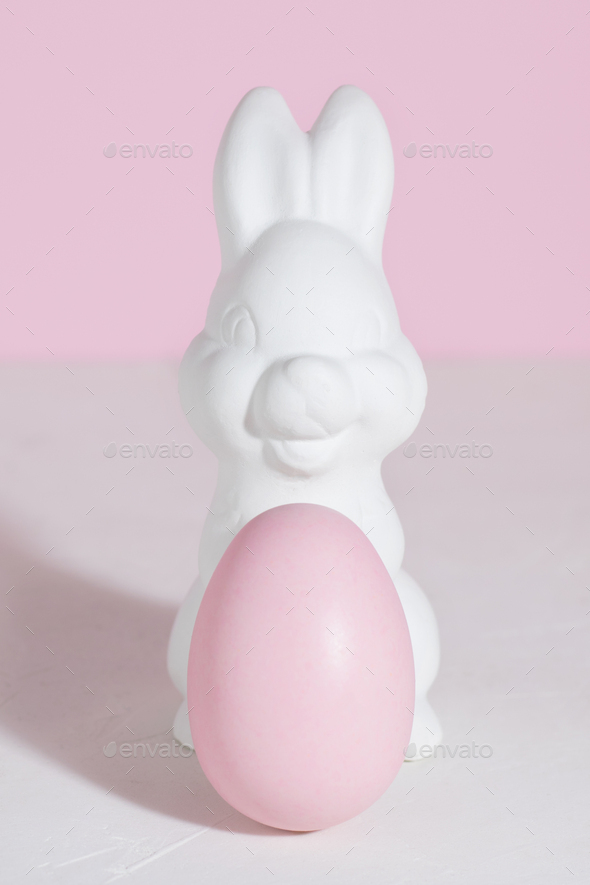 White Easter bunny with a pink Easter egg on a concrete table, on a ...