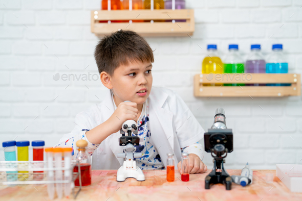 Young boy wear lab gown and work with microscope in science class of ...