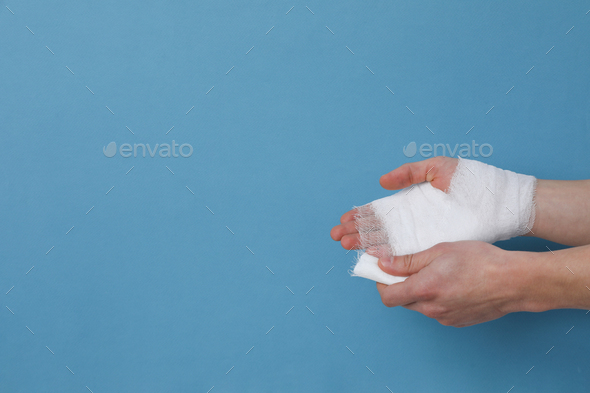 Concept of help during an injury, man wrapping hand in bandage on blue ...