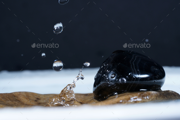 Closeup shot of shiny obsidian rock in water with droplets of water ...
