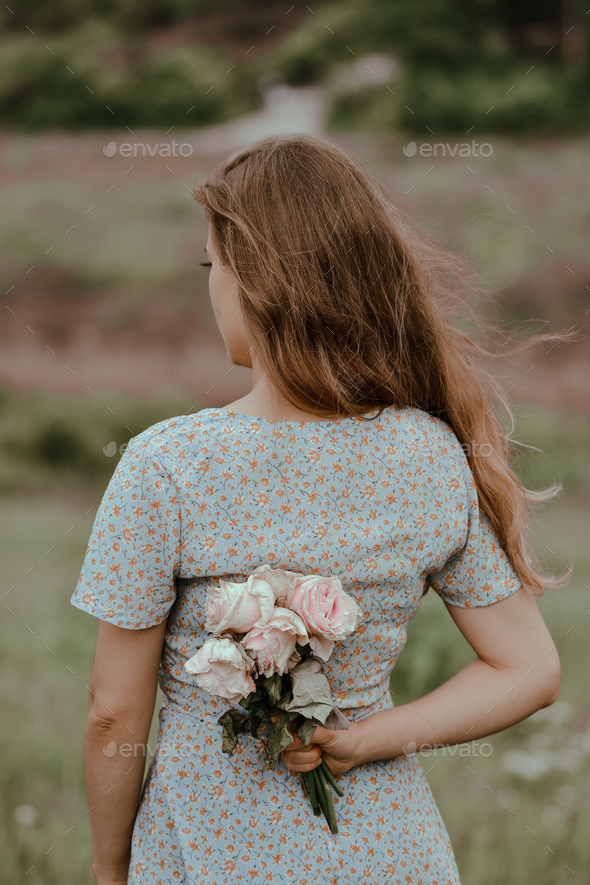 Young girl wearing a beautiful dress holding a bouquet of roses behind ...