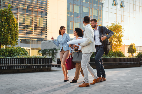 Group of coworkers walking outside in front of office buildings discuss ...
