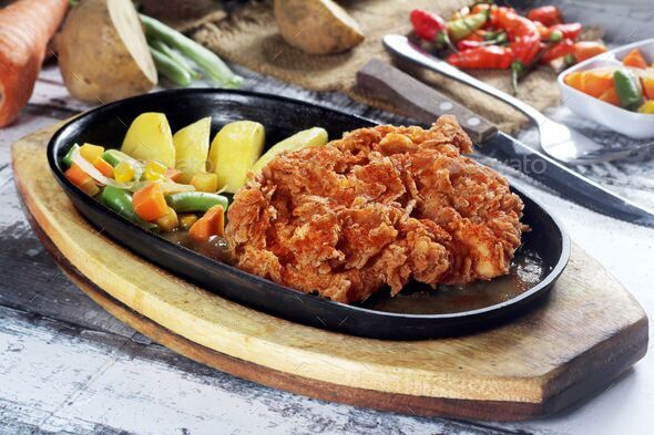 Closeup of crispy chicken steaks in sauce with steamed vegetables on a ...