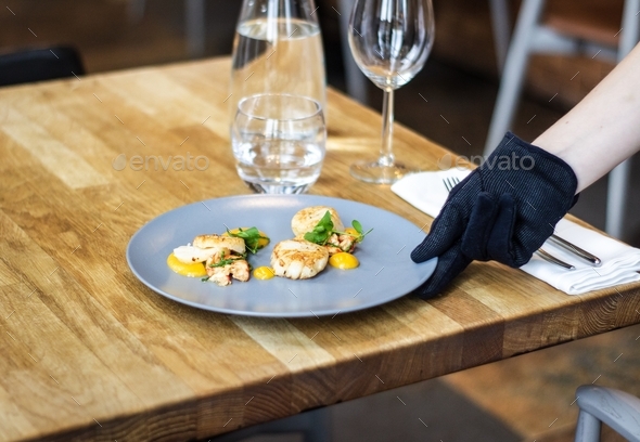Waiter putting down the dish on a wooden table with a blurred ...