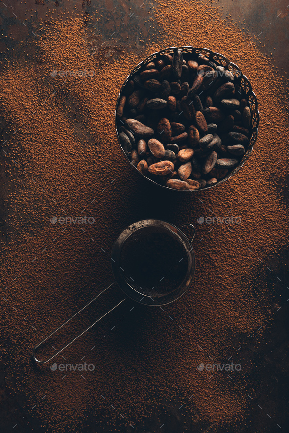 top view of gourmet cocoa beans in vintage bowl and sieve on cocoa ...