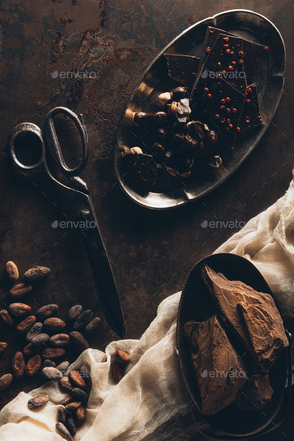 top view of vintage scissors, cocoa beans, cloth, chocolate pieces and ...