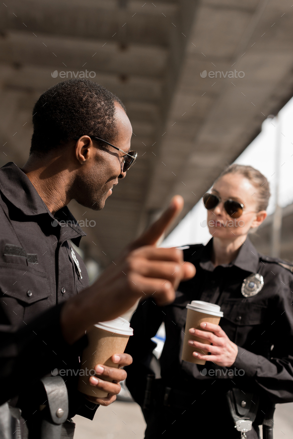 policeman pointing somewhere while drinking coffee to go with partner ...