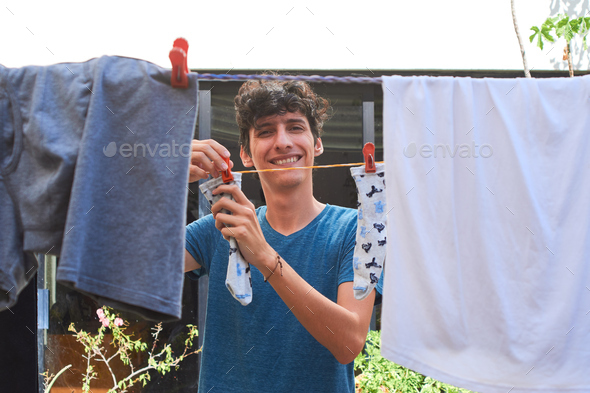 Young adult male dries clothes on clothesline ropes in backyard. Stock ...