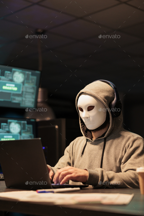Masked scammer hacking computer network at night Stock Photo by DC_Studio