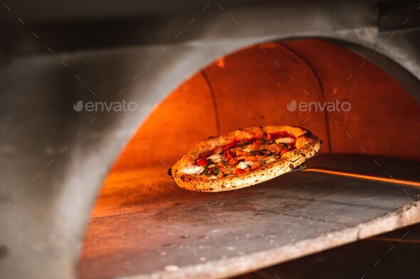 Closeup shot of pulling baked Neapolitan pizza out from an oven with ...