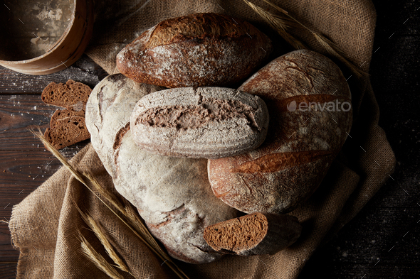 elevated view of various types of bread, wheat, sieve and sackcloth on ...