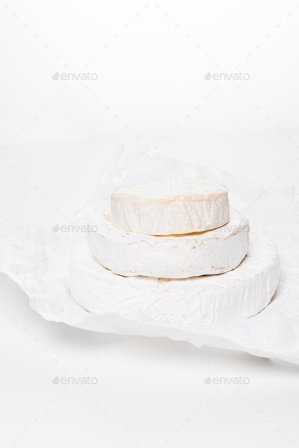 stack of tasty brie cheese heads on crumpled paper and on white surface ...