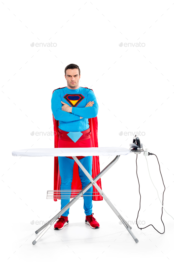 handsome superman standing with crossed arms near ironing board and ...