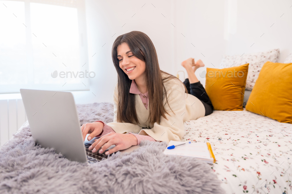 Young woman using her laptop personal computer in bed, millennial ...