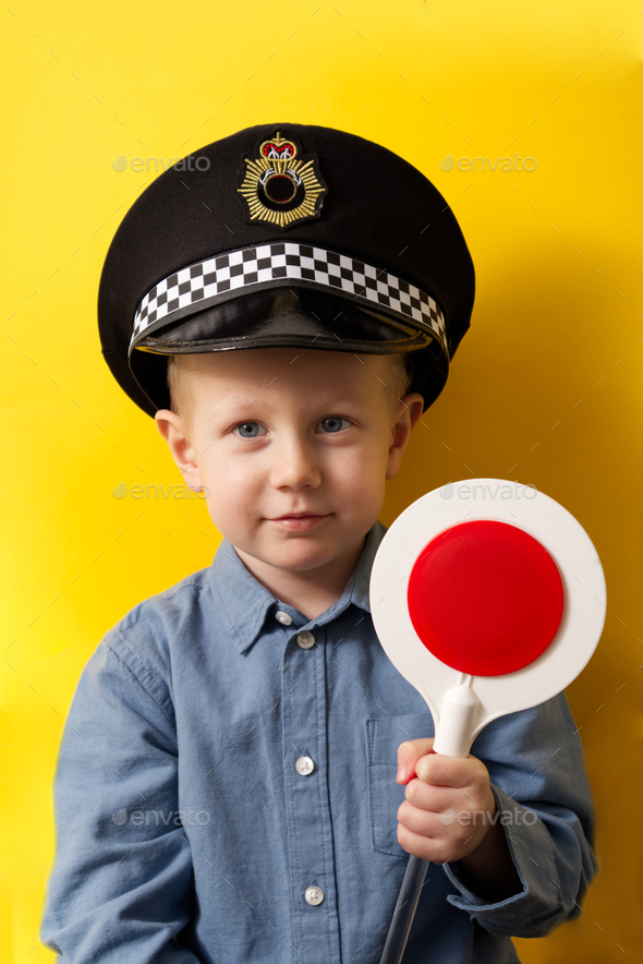 Boy in a cap of a policeman showing a red traffic light on a yellow ...