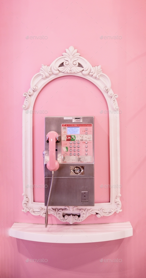 Vertical shot of a pink cabin telephone inside a white frame on a pink ...