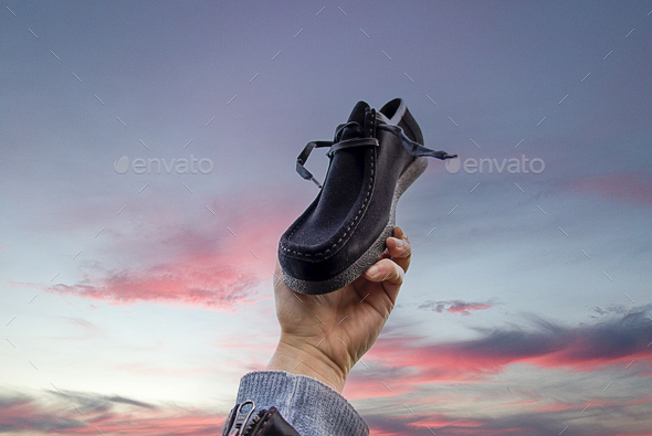 Closeup of a hand holding a beautiful black shoe in the sunset sky ...